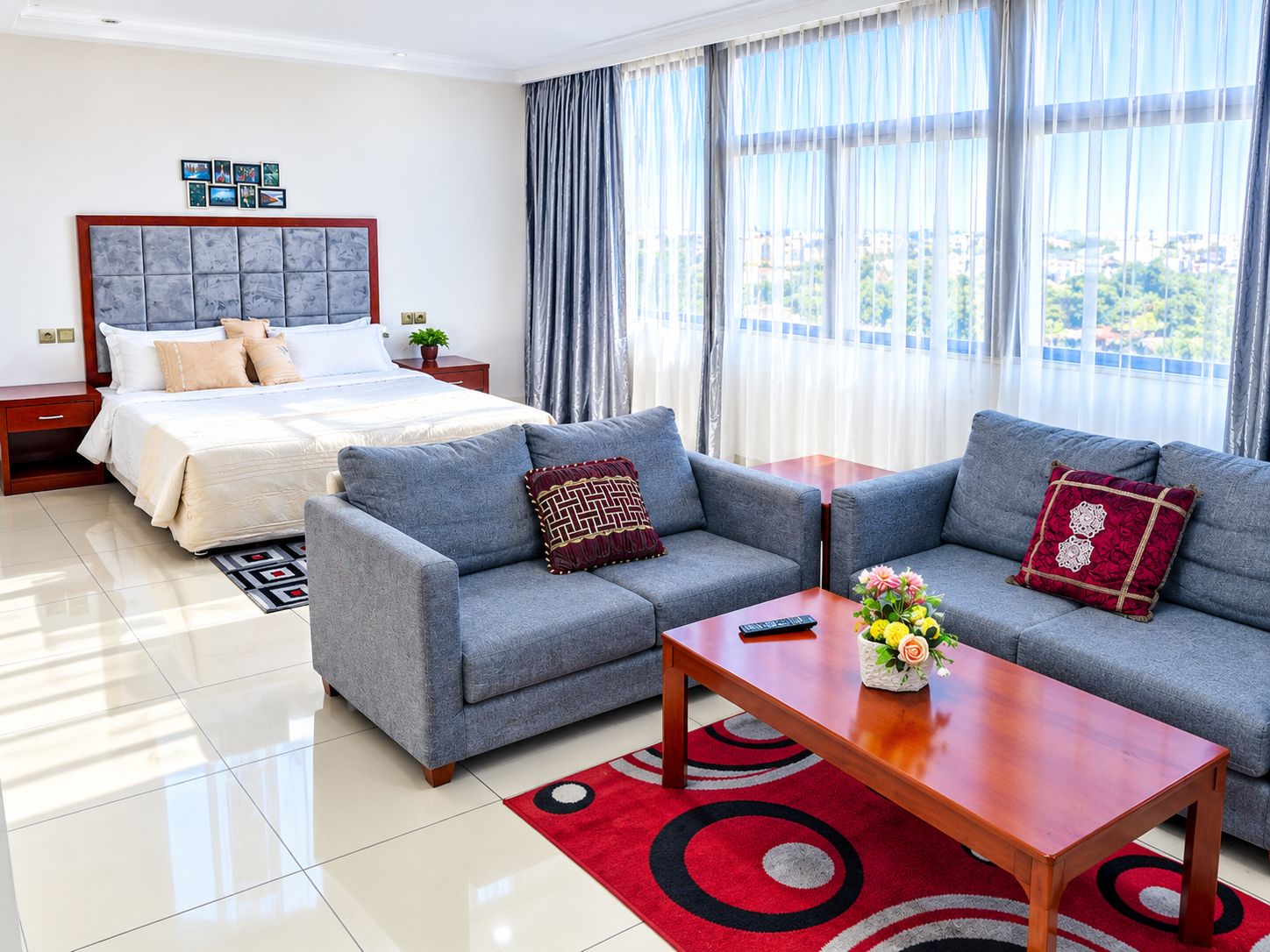 Quarto de hotel com uma cama, dois sofás, uma mesa de centro e vista da cidade através de grandes janelas.