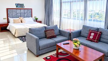Quarto de hotel com uma cama, dois sofás, uma mesa de centro e vista da cidade através de grandes janelas.