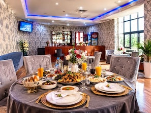 Uma área de refeições com um bar ao fundo, apresentando diversos pratos e bebidas na mesa.