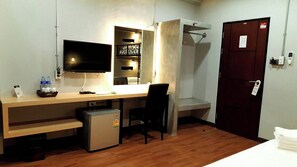 Quarto de hotel com cama, escrivaninha com computador, televisão, minibar e chuveiro.
