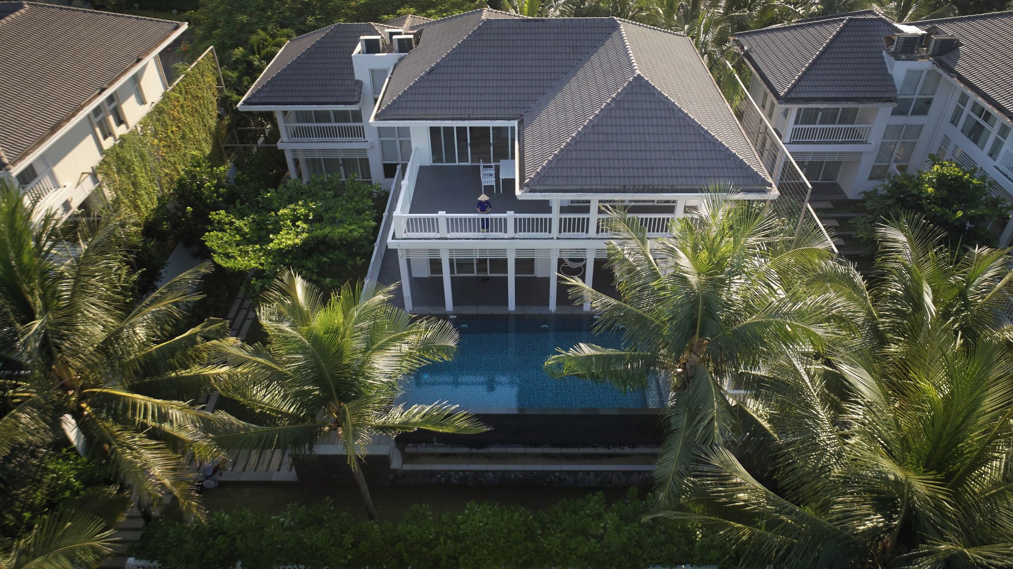 Uma casa grande com piscina, rodeada por palmeiras.