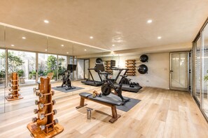 Uma academia ampla com equipamentos de ginástica, grandes janelas e piso de madeira.