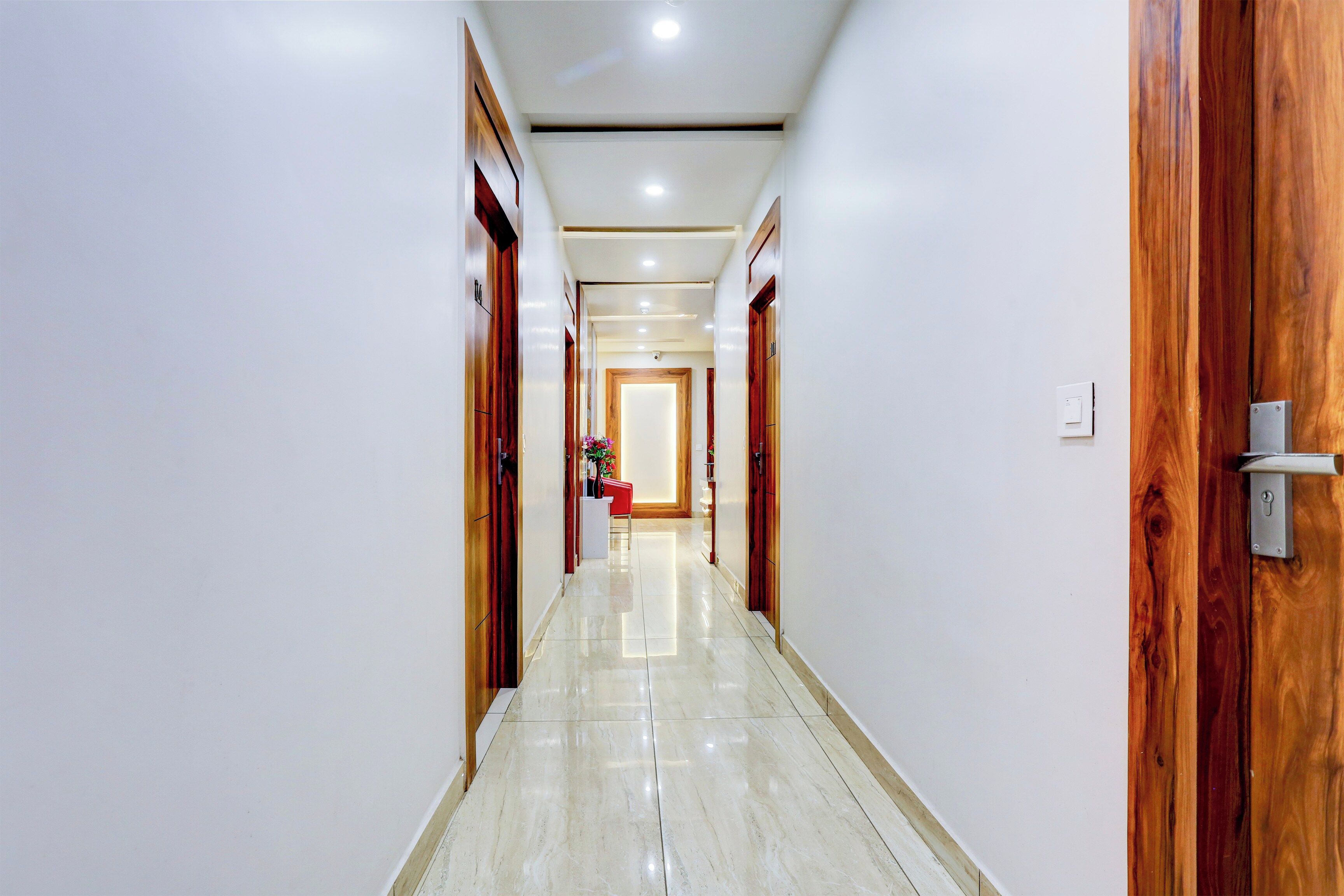 Um corredor com portas de madeira, piso ladrilhado e uma cadeira vermelha ao fundo.