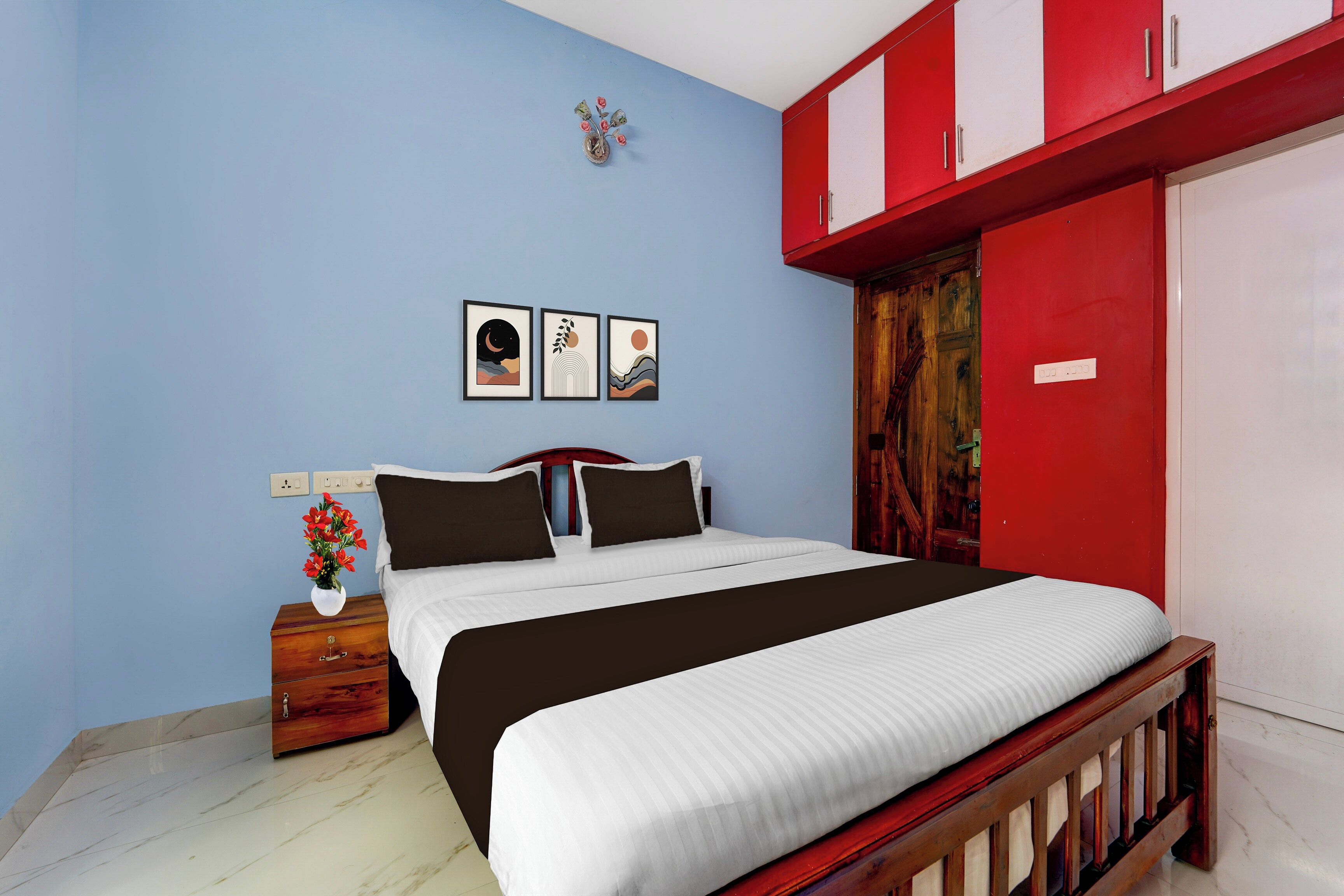 Quarto com cama, mesa de cabeceira, penteadeira e guarda-roupa. Há três quadros na parede.