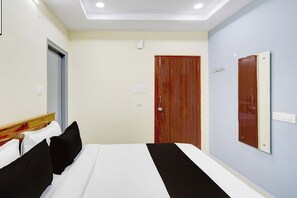 Quarto de hotel com cama, porta de madeira, cabideiro e espelho na parede.