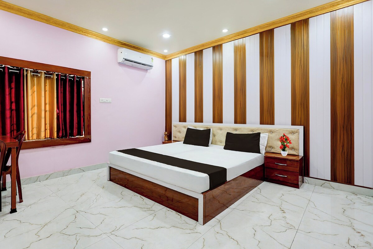 Quarto com cama grande, cabeceira de madeira, mesa de cabeceira, cortina vermelha e ar condicionado fixado na parede.