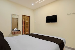 Quarto de hotel com cama, televisão fixada na parede, espelho e guarda-roupa de madeira.