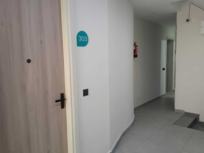 Corredor com uma porta identificada com o número '303' e um extintor de incêndio fixado na parede.