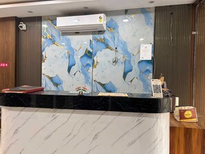 Balcão de recepção com bancada de mármore, ar-condicionado fixado na parede e parede decorativa com padrão semelhante ao mármore.