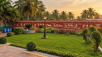 Um jardim bem cuidado com um muro decorativo, palmeiras e um caminho.