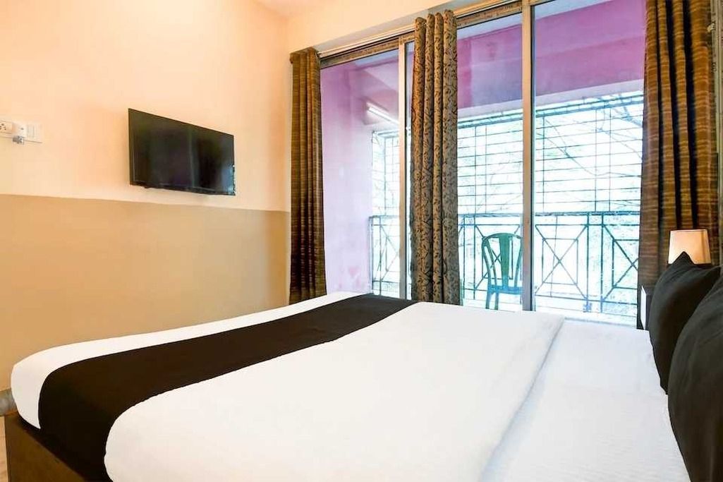 Quarto de hotel com uma cama, televisão na parede e varanda com cortinas.