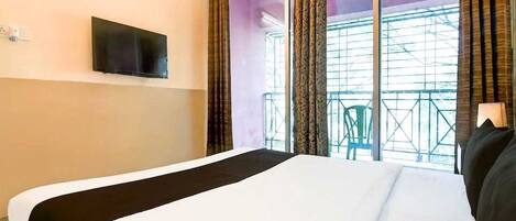 Quarto de hotel com uma cama, televisão na parede e varanda com cortinas.