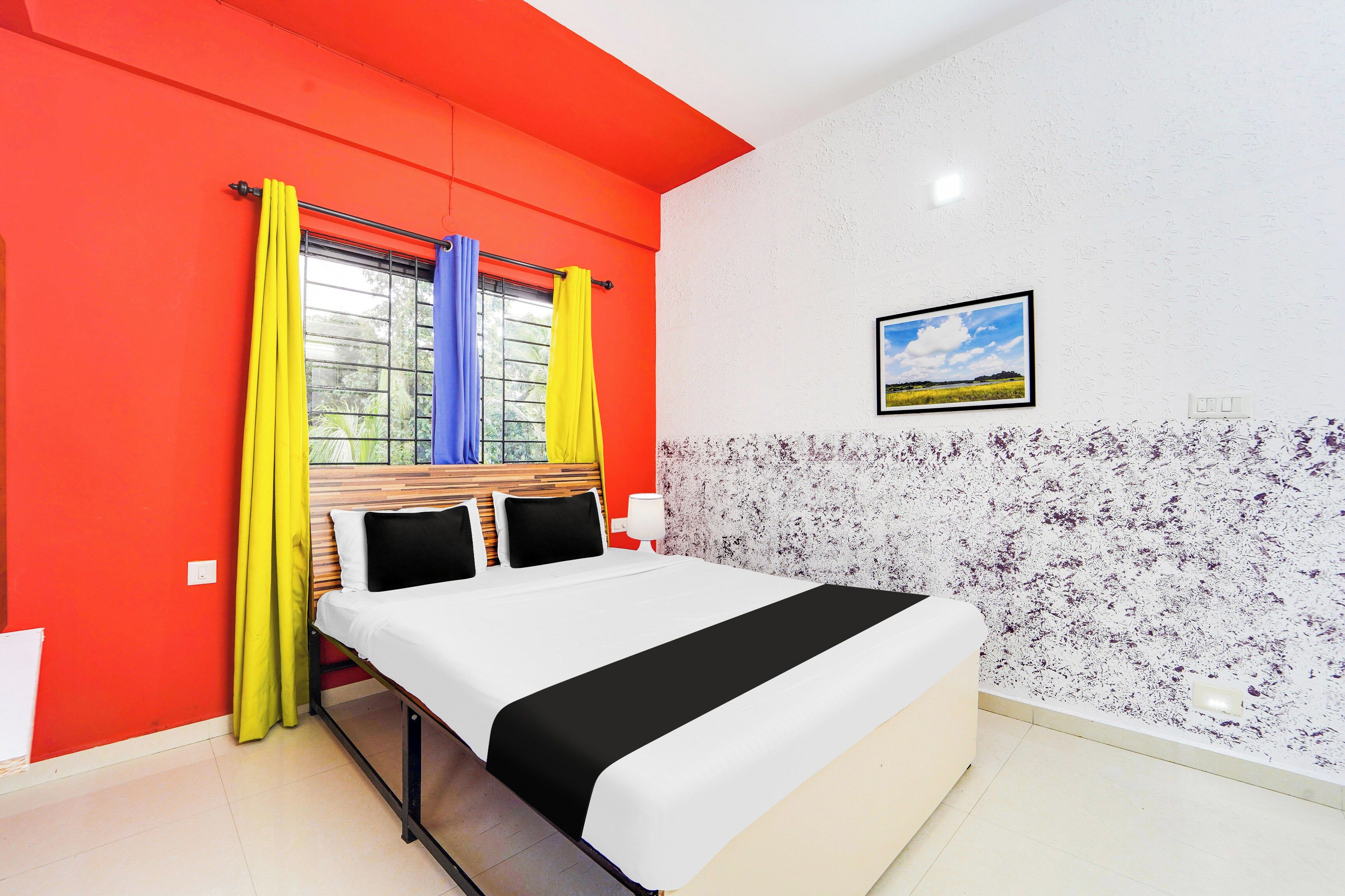 Quarto com cama, cortinas, janela com vista, um quadro na parede e um interruptor de luz.
