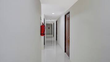 Um corredor com paredes brancas, um extintor fixado na parede e portas do lado direito.