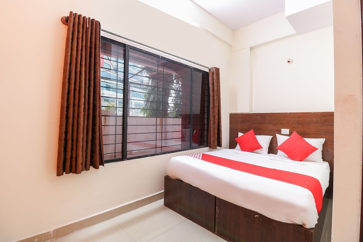 Quarto com cama, janela com cortinas e vista de um edifício.