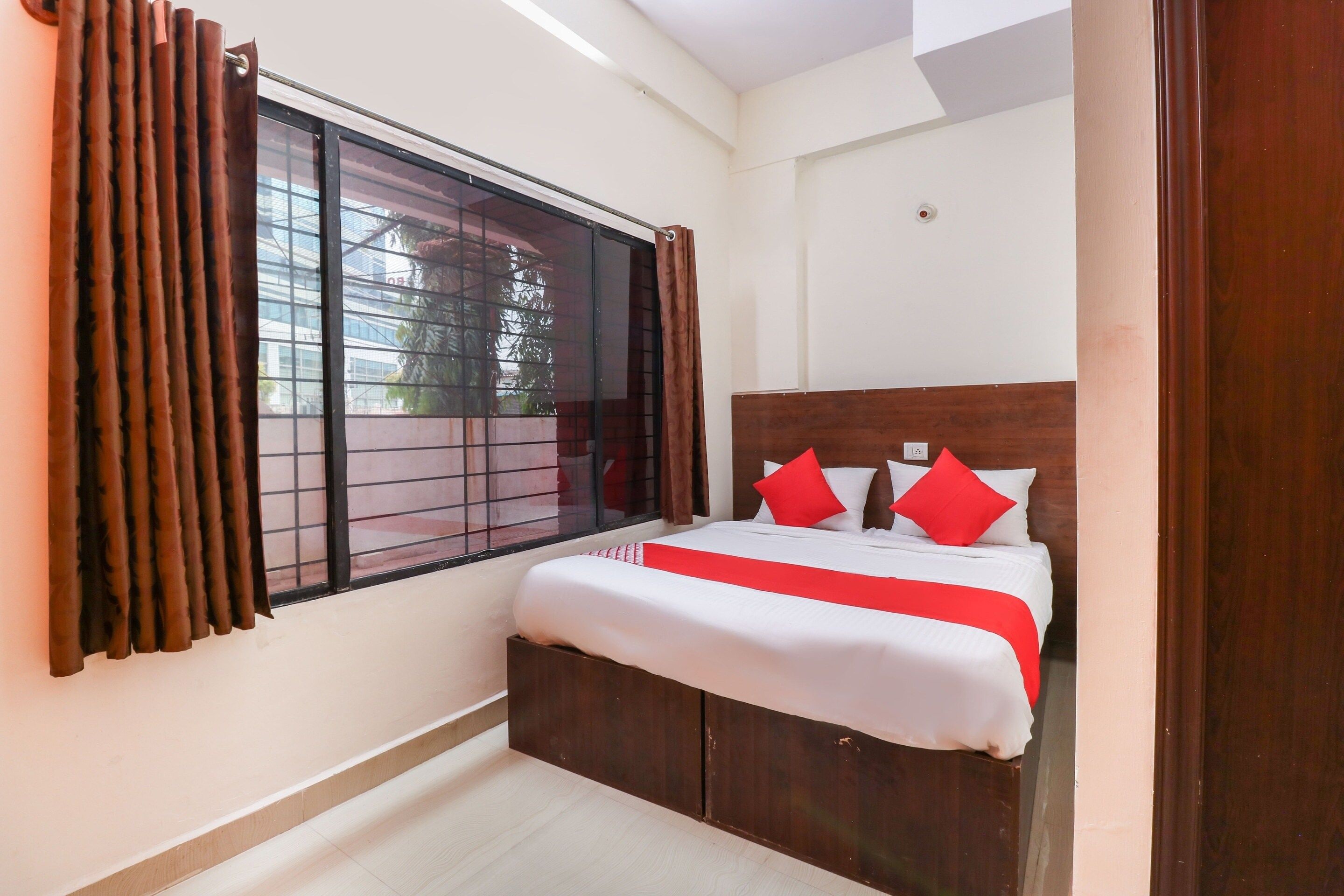 Quarto com cama, janela com cortinas e vista para um prédio.