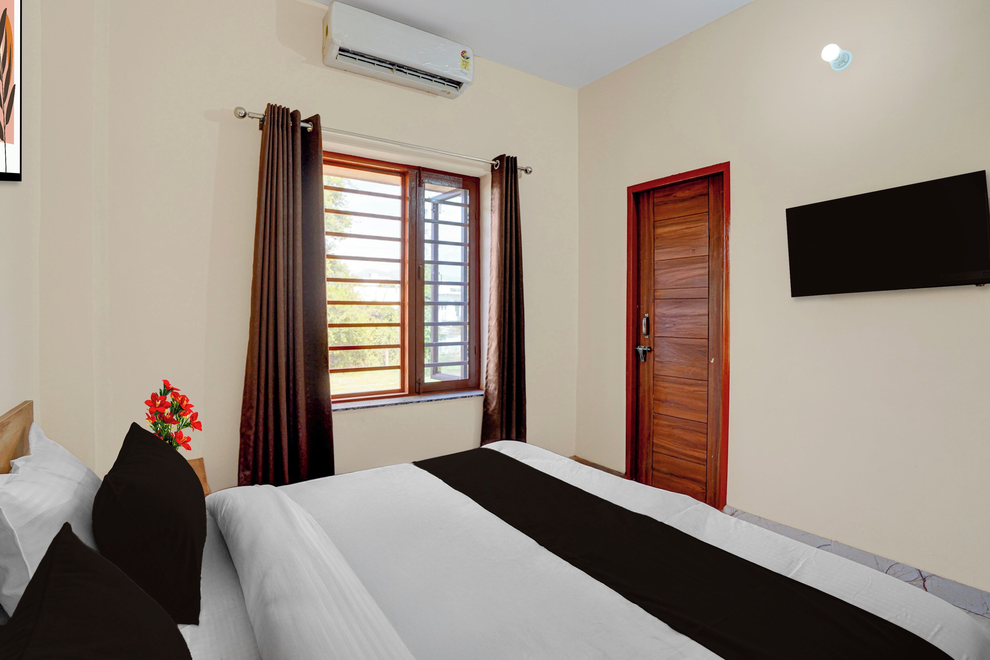 Quarto de hotel com cama, janela com cortinas, ar condicionado, porta e televisão de tela plana fixada na parede.