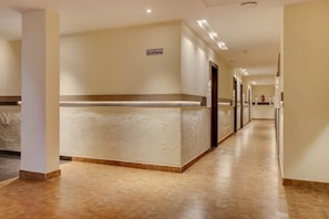 Recepção de hotel com balcão de atendimento, placa de 'Proibido Fumar' e corredor com portas numeradas.