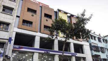 Um edifício com vários andares e espaços comerciais no andar térreo, incluindo uma loja da TVS e uma agência do Axis Bank.