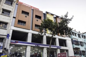 Um edifício com vários andares e espaços comerciais no andar térreo, incluindo uma loja da TVS e uma agência do Axis Bank.