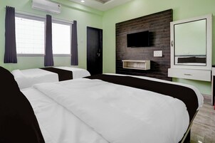 Quarto de hotel com duas camas, televisão, espelho e janela com cortinas.