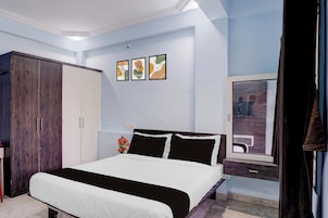 Quarto com cama, guarda-roupa, espelho e três quadros na parede.