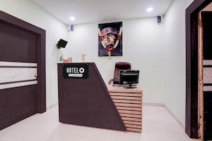 Uma área de recepção de hotel, com balcão, computador e um quadro na parede.
