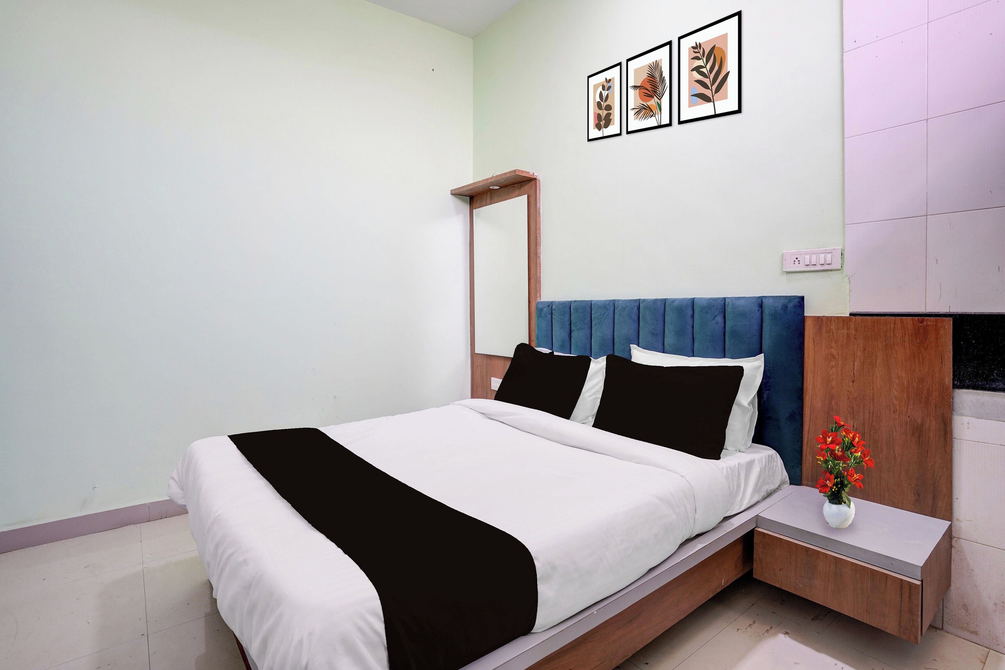 Cama bem arrumada com colcha preta e branca, cabeceira de madeira e mesa de cabeceira com um vaso de flores.