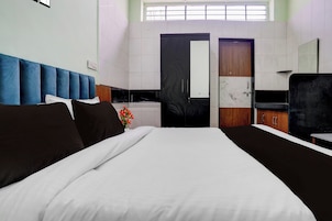 Quarto de hotel com uma cama grande, cabeceira azul, banheiro com espelho e uma janela.