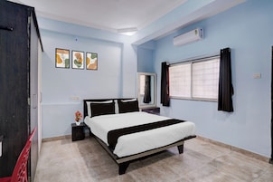 Quarto com cama, mesa de cabeceira, espelho, ar condicionado e janela com cortinas.
