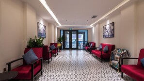 Um saguão de hotel com assentos vermelhos, piso estampado e obras de arte nas paredes.