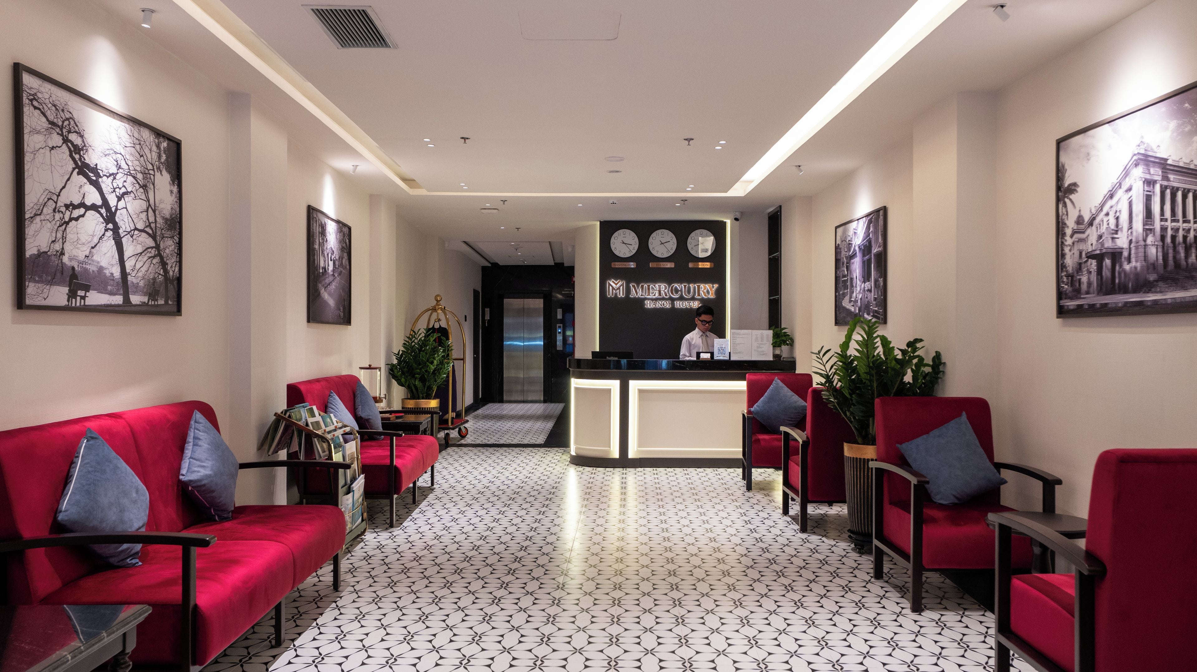 Uma área de recepção de hotel com balcão, assentos vermelhos e obras de arte emolduradas nas paredes.