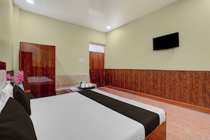Quarto de hotel com cama, sofá, armário de madeira, televisão fixada na parede e janela com cortinas.