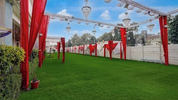 Espaço ao ar livre com cortinas vermelhas, um toldo branco e lustres pendurados.
