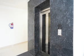Um elevador moderno com parede de mármore, um extintor de incêndio fixado na parede e um painel de comando.