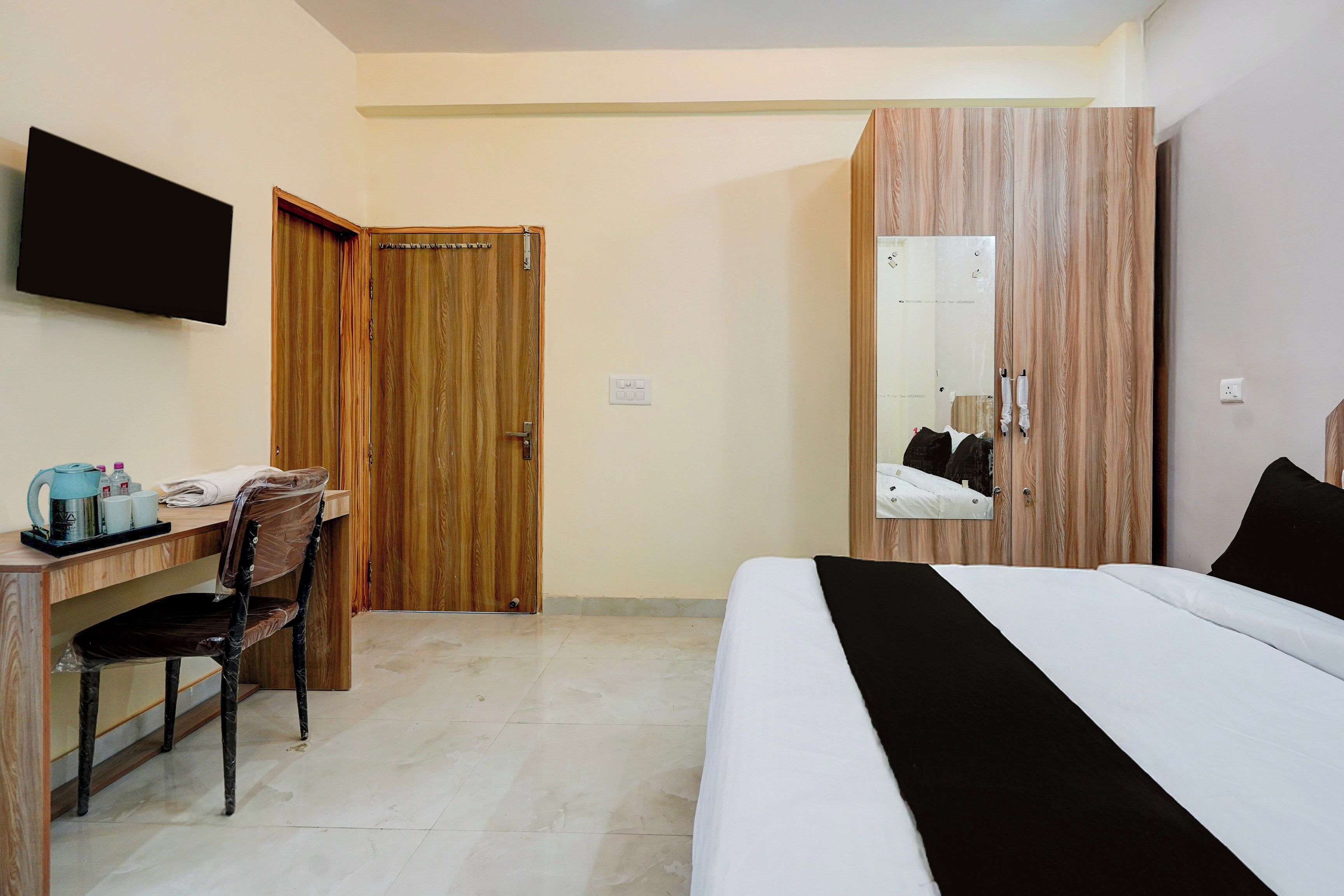 Quarto de hotel com cama, escrivaninha e cadeira, televisão na parede e guarda-roupa de madeira.