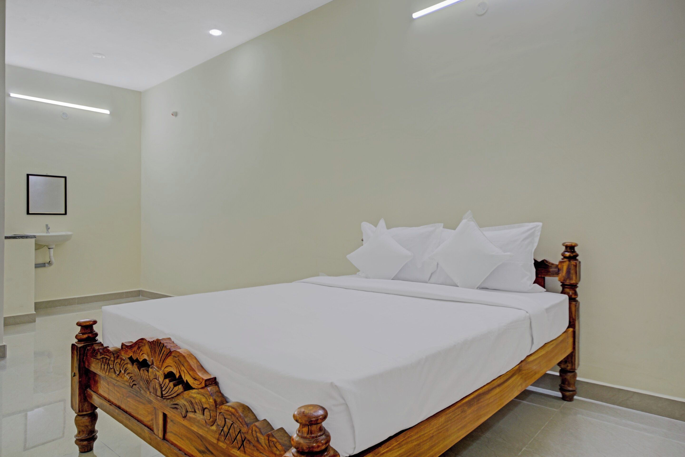 Cama bem arrumada em quarto de hotel, com cabeceira de madeira, parede branca e pequena mesa de cabeceira.