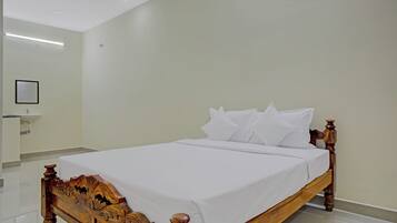 Cama bem arrumada em quarto de hotel, com cabeceira de madeira, parede branca e pequena mesa de cabeceira.