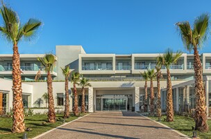 Um hotel moderno com entrada central, vários andares e palmeiras ao longo do caminho.