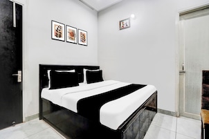 Quarto com cama de estrutura preta, roupa de cama branca e três obras de arte emolduradas na parede.