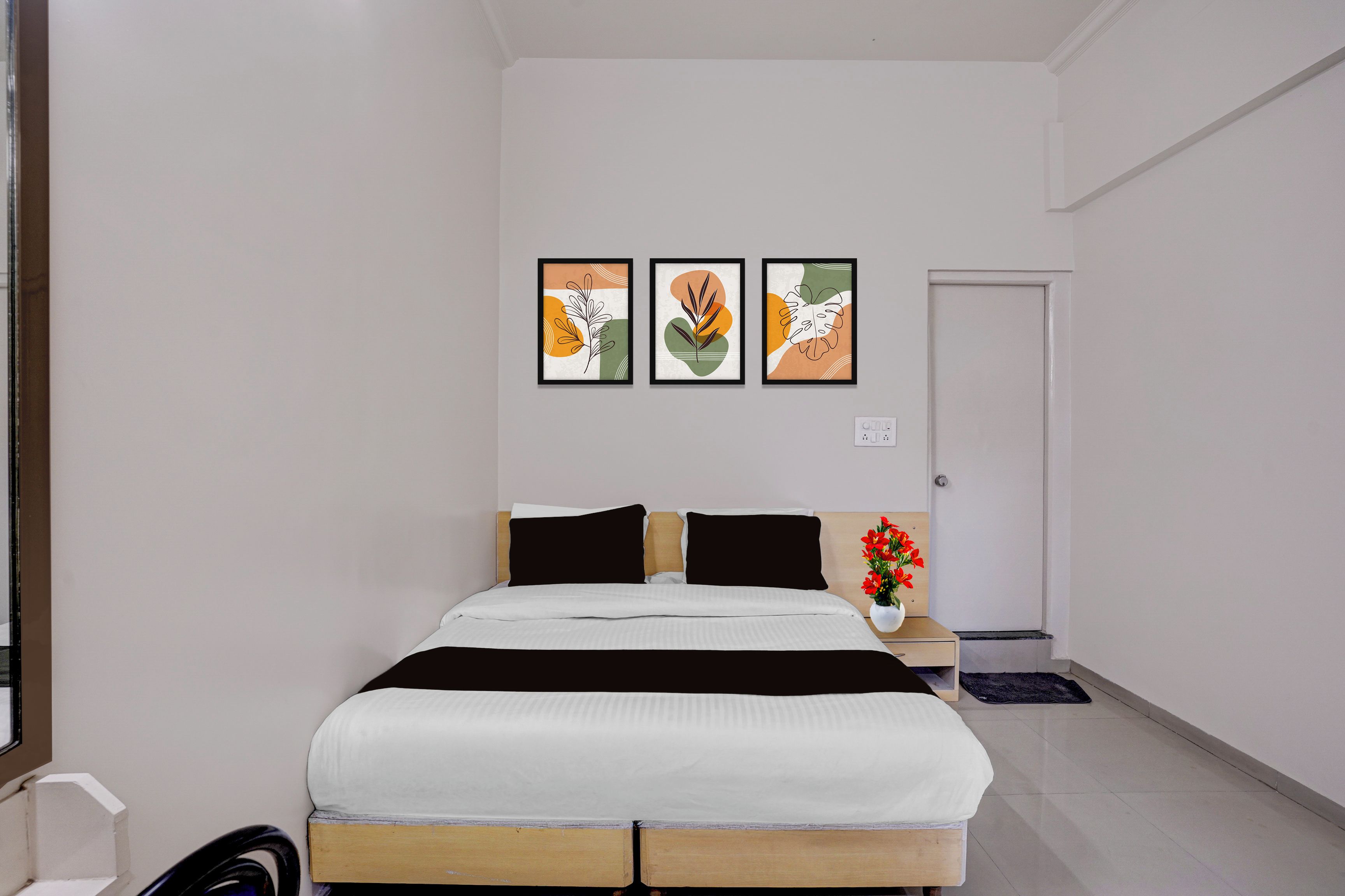 Quarto com cama, mesa de cabeceira, vaso com flores e três quadros na parede.