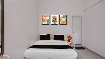 Quarto com cama, mesa de cabeceira, vaso com flores e três quadros na parede.