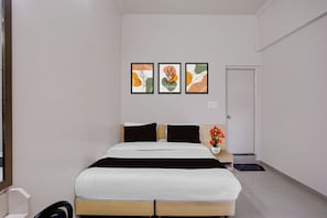 Quarto com cama, mesa de cabeceira, vaso com flores e três quadros na parede.
