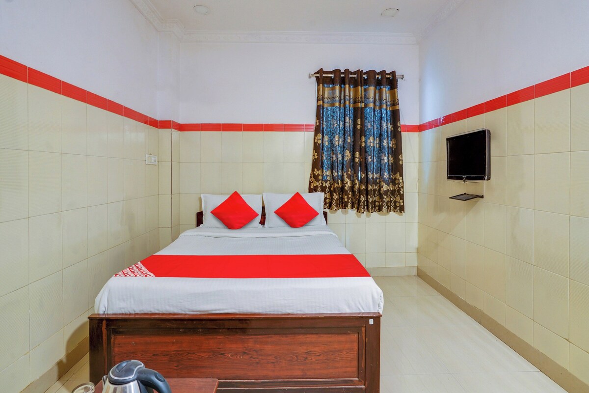 Quarto de hotel com cama, televisão presa na parede e janela com cortinas.