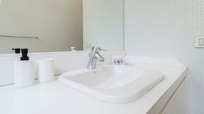 Casa de banho com lavatório branco, espelho e artigos de higiene pessoal.