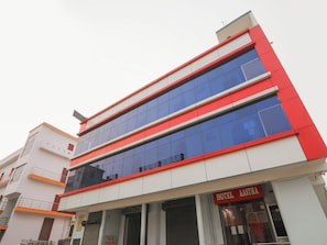 Um hotel de vários andares com fachada em vermelho e branco, grandes janelas de vidro e uma placa visível com o nome 'AASTHA'.