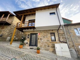 Um edifício de dois andares com fachada de pedra, varanda de madeira e porta preta com placa de número.