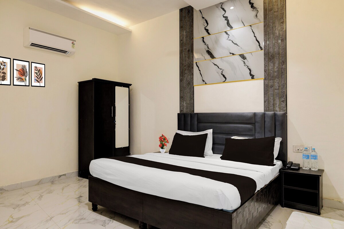 Quarto de hotel com cama, mesa de cabeceira, garrafa de água e ar-condicionado fixado na parede.