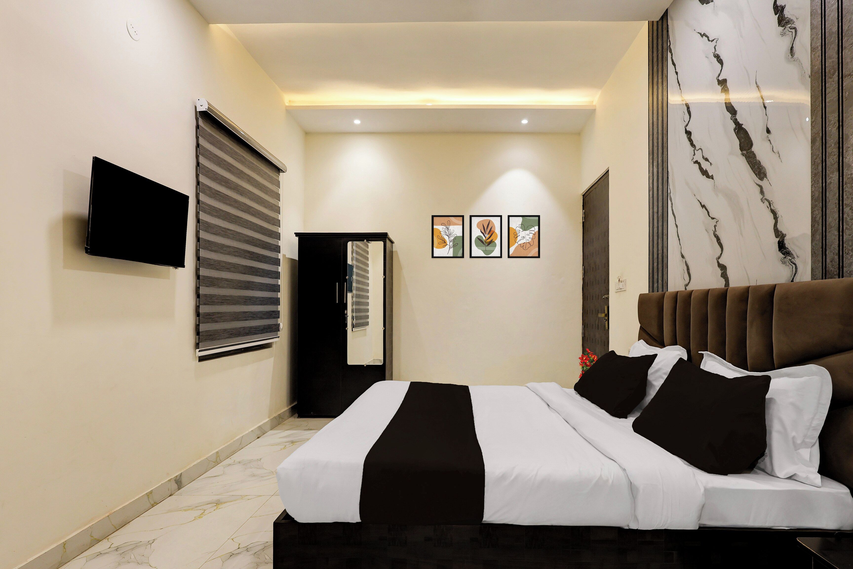 Quarto moderno com cama, televisão, uma porta e três obras de arte emolduradas na parede.