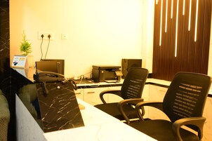 Uma área de recepção com balcão de mármore, duas cadeiras de escritório pretas, uma mesa com um computador e um vaso de planta.